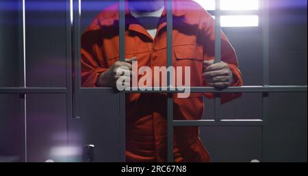 Elderly prisoner in orange uniform stretches fingers, leans on metal ...