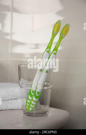 Light green toothbrushes in glass holder, terry towel and rosemary on ...