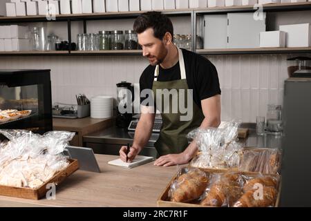 Happy seller writing something at cashier desk in bakery shop Stock ...