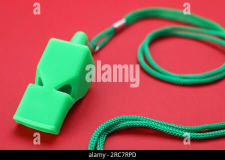 One green whistle with cord on red background, top view. Space for text ...