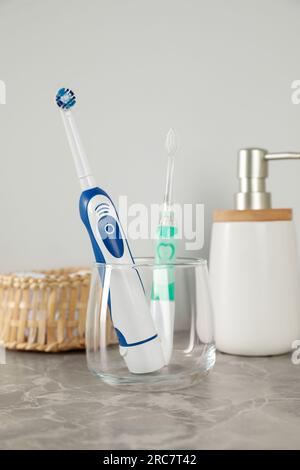 Electric toothbrushes in glass on light grey marble table Stock Photo ...