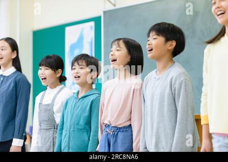 Elementary school students singing a song in front of the blackboard ...