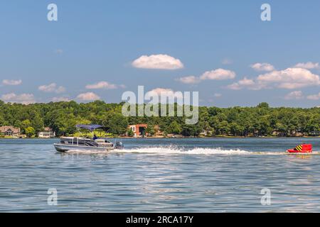 Pontoon boat pulling inflatable tube float raft on lake. Family on a ...