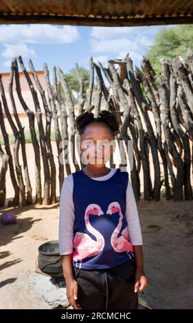 African village child standing under the shade in the shack, outdoors ...