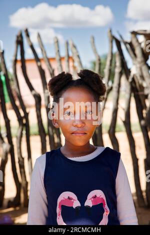 African village child standing under the shade in the shack, outdoors ...