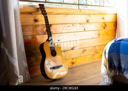 Acoustic guitar leaning against wood panelled wall below window in ...