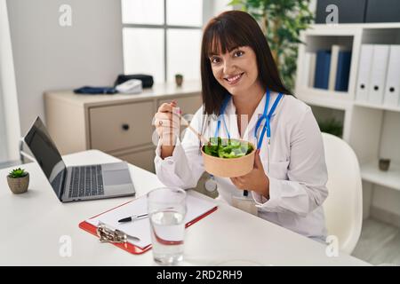 Smiling doctor sitting with laptop by salad box at desk Stock Photo - Alamy