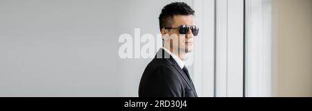 good looking bodyguard in sunglasses, handsome man in suit touching ...