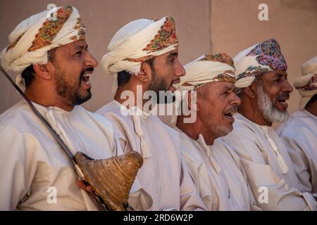 A group of Omani men in traditional Dishdash dress meeting in front of ...