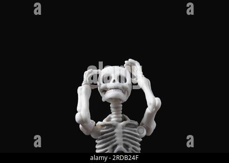 Skeleton figurine hold head by black background. Desperate figure on ...