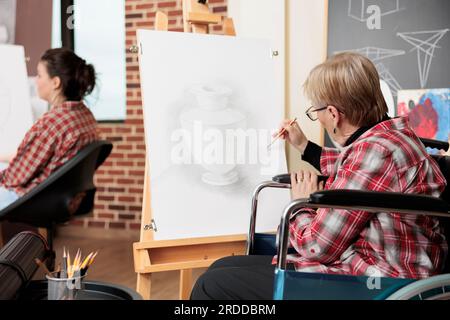 Female art student in wheelchair making pencil sketch on blank canvas ...