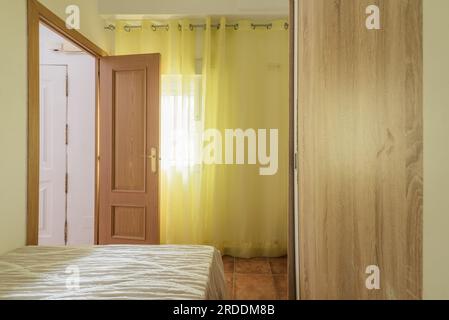Spartan bedroom with a simple bed, an orange cushion and a wardrobe ...