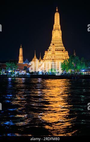 Illuminated pagoda reflecting on the water at night with city lights in ...