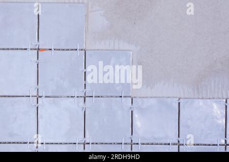 A portrait of an unfinished ceramic tile wall, with white plastic joint ...