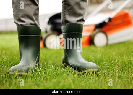 Cropped photo of male gardener legs in rubber boots stands on cut green ...
