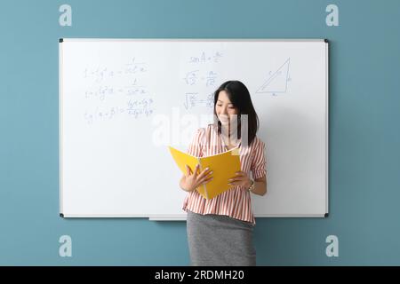 Asian Math teacher with notebook near flipboard in classroom Stock ...