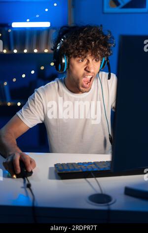 Shocked young arabic gamer wearing headphones screaming playing video ...