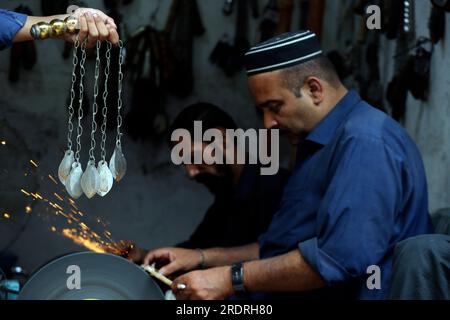 A Pakistani iron smith sharpens knives, as bunches of knives and chains ...