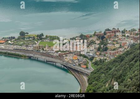 The top view of Lake Lugano and Melide Causeway through the tall green ...