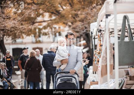 Father walking carrying his infant baby boy child and pushing stroller ...