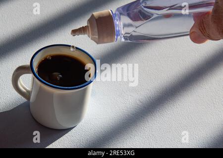 person sweetening coffee with liquid sweetener, scene showing cup and ...