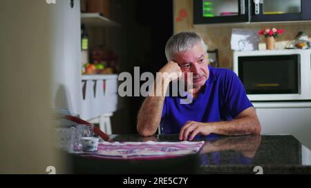 Preoccupied senior man at kitchen table ruminating problems, candid ...