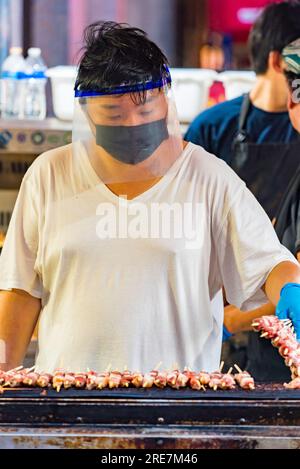 A person wearing a cloth and plastic shield mask while cooking ...
