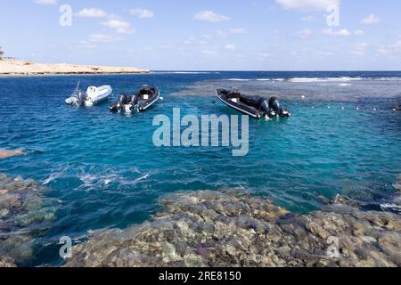 Three inflatable boats sit empty at anchor on a coral reef with crystal ...