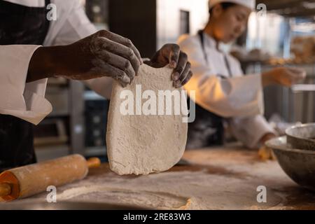 Focused diverse bakers wearing aprons in bakery kitchen, holding ...