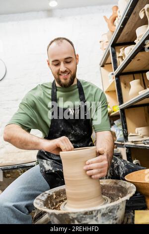 Smiling man forming clay sculpture near blurred african american ...