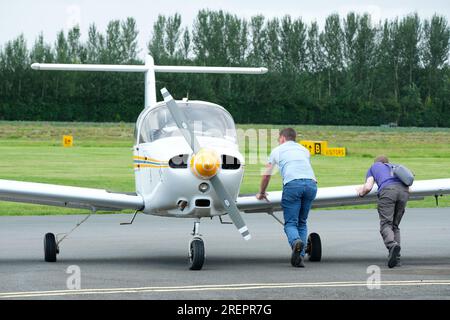 Pilot pushing a Piper Pa-38 Tomahawk light aircraft at a small general ...