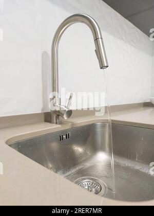 A kitchen sink with an open faucet with running water and a mountain of ...