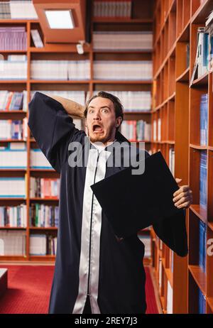 Shocked graduate wearing his cap and gown pumps his fist in the air and ...
