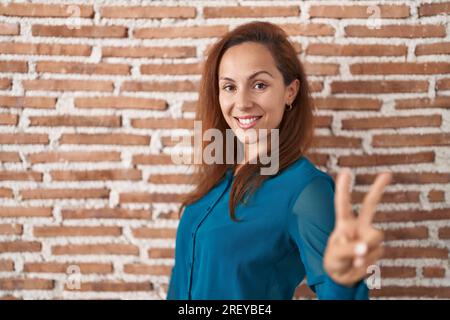 Brunette woman standing over bricks wall relaxed with serious ...