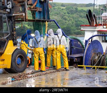 Fishermen loading nets onto a trawler using forklift truck and ...