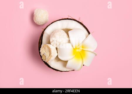 Coconut with white chocolate candies and plumeria flower on pink ...