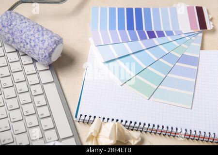 Color palettes, PC keyboard, paint roller and notebook on light ...
