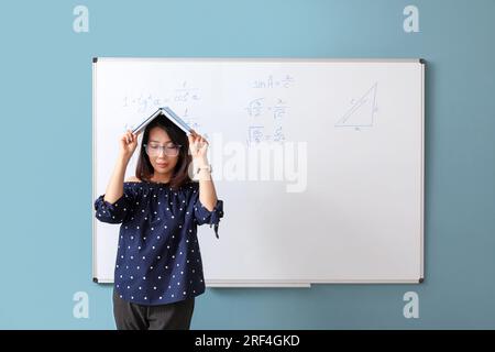 Asian Math teacher with book near flipboard in classroom Stock Photo ...