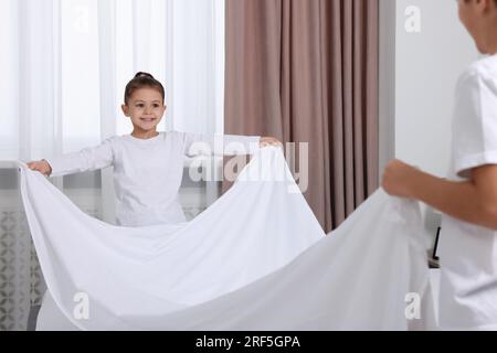 Brother and sister changing bed linens together in bedroom Stock Photo ...