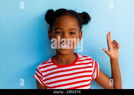 African american schoolgirl doing sign language with hand over blue ...