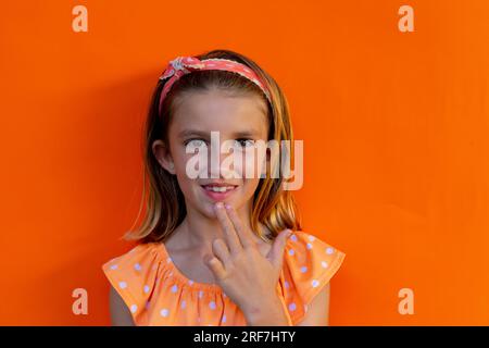 Caucasian schoolgirl doing sign language gesture over blue background ...