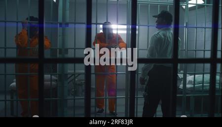 Jailer with police baton stands in front of jail cells and talks with ...