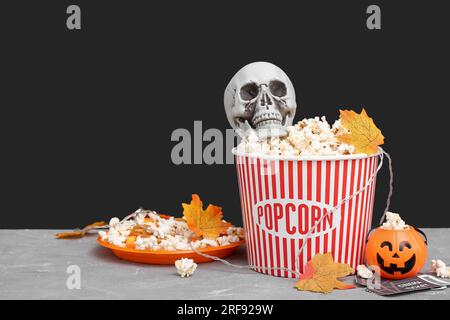Bucket with tasty popcorn, skull and cinema tickets on grey table ...