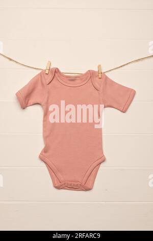 Pink baby grow hanging with clothes pegs with copy space on white ...