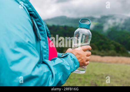 caucasian 50s blonde girl drinking water from plastic bottle. Mountain ...