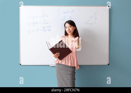Asian Math teacher with book near flipboard in classroom Stock Photo ...