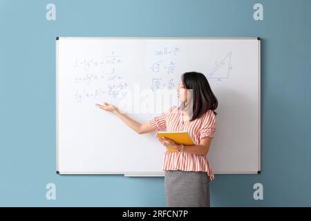 Asian Math teacher with notebook near flipboard in classroom Stock ...