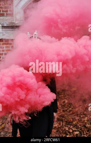 A woman in the guise of Baron Sabbath poses in red smoke. Smoke covers ...