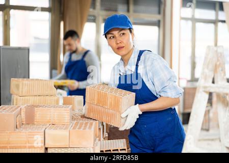 Female builder preparing red bricks in building under reconstruction ...