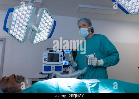 Caucasian male surgeon using defibrillators on african american patient ...